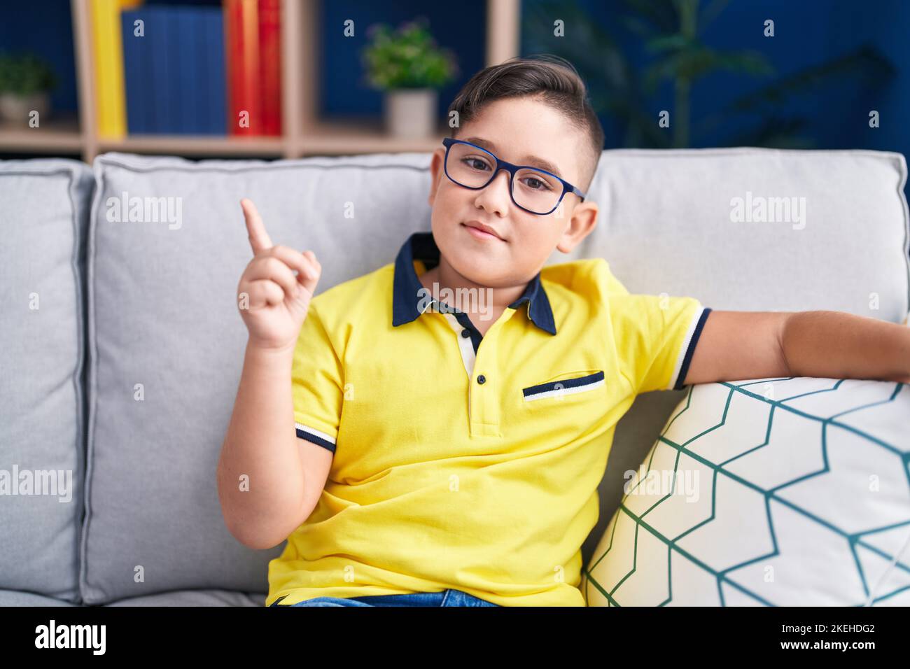 Young hispanic kid sitting on the sofa at home smiling happy pointing ...