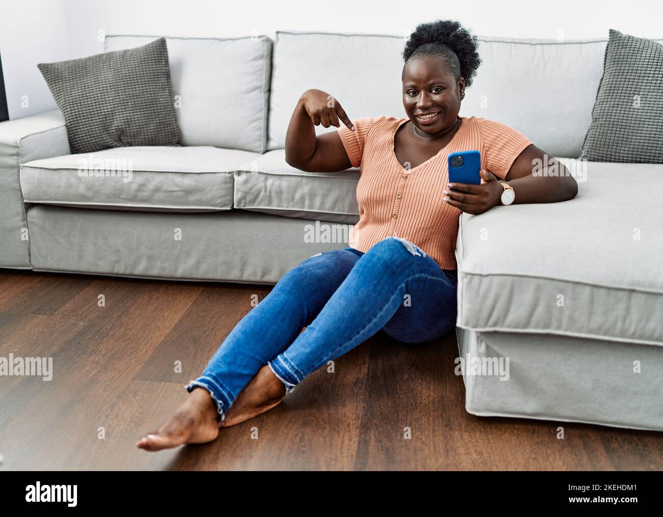 Young african woman using smartphone sitting on the floor at home ...
