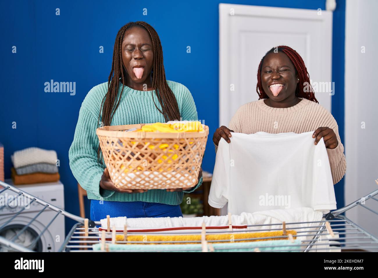 Two african women hanging clothes at clothesline sticking tongue out ...