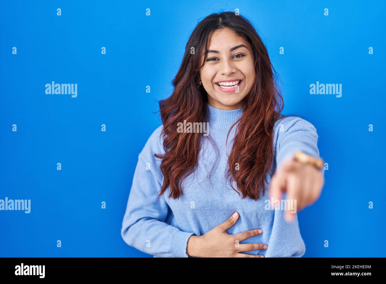 Hispanic young woman standing over blue background laughing at you ...
