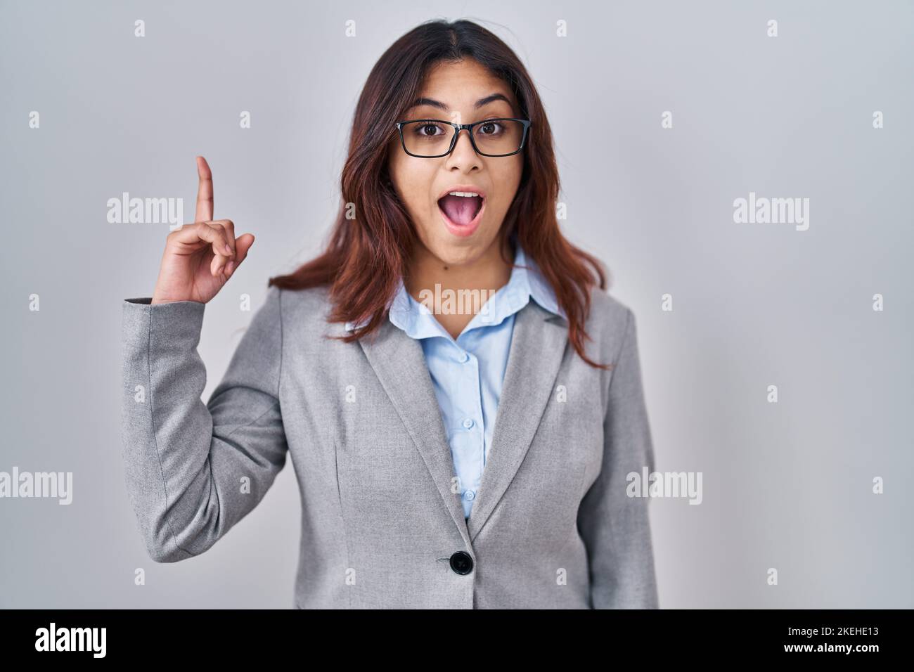 Hispanic young business woman wearing glasses pointing finger up with ...
