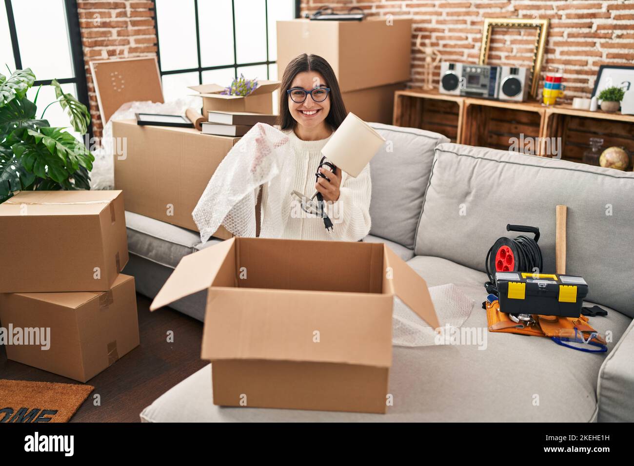 Young hispanic woman smiling confident unpacking cardboard box at new ...