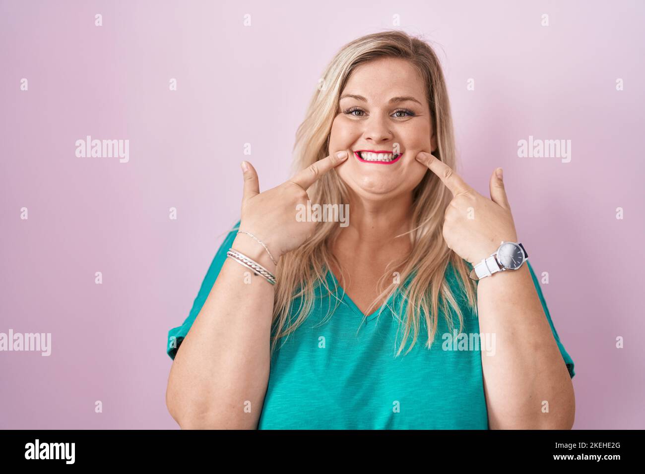 Caucasian plus size woman standing over pink background smiling with ...