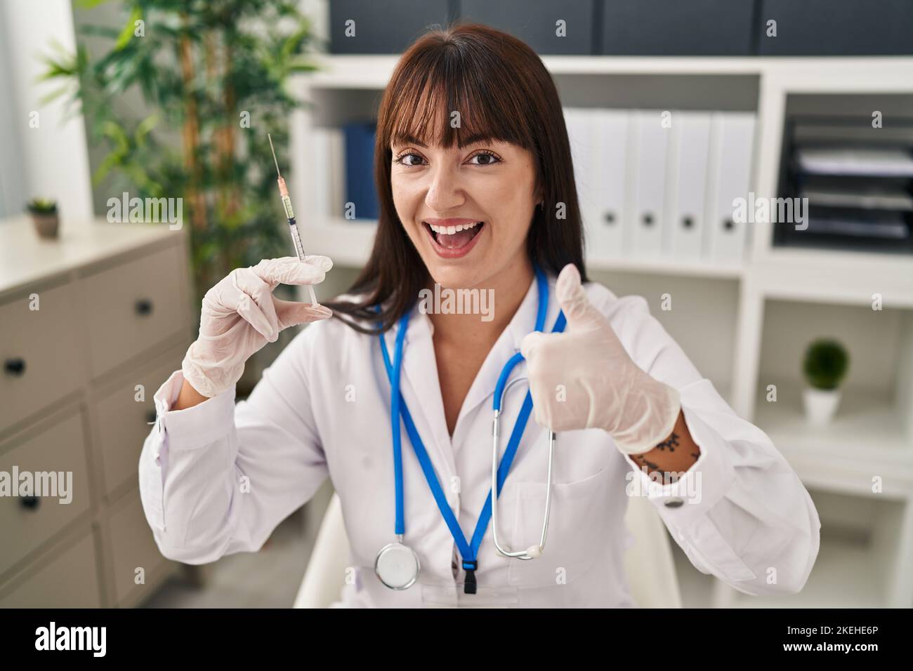 Young brunette doctor woman holding syringe smiling happy and positive ...