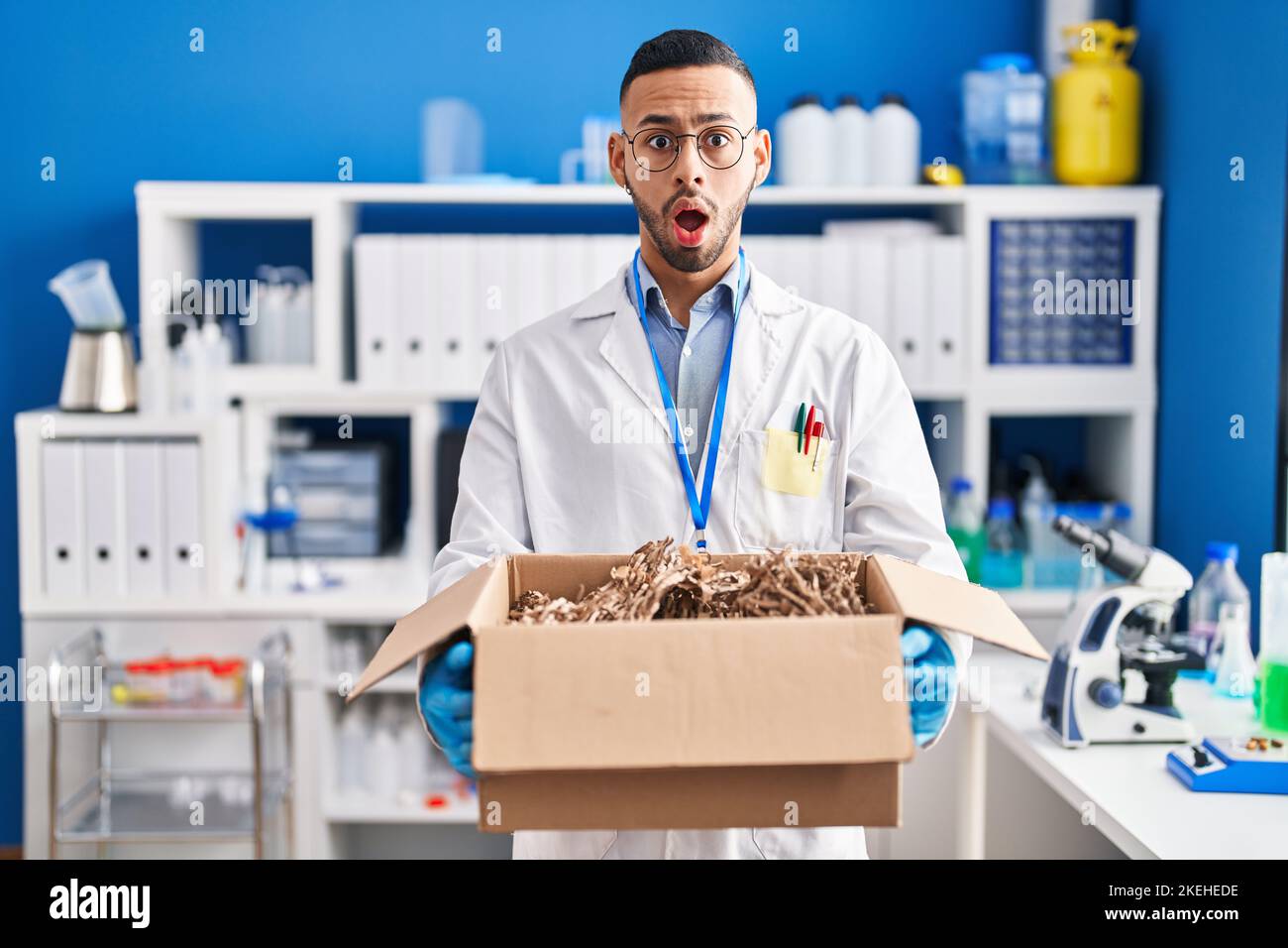 Young hispanic man working at scientist laboratory holding cardboard ...