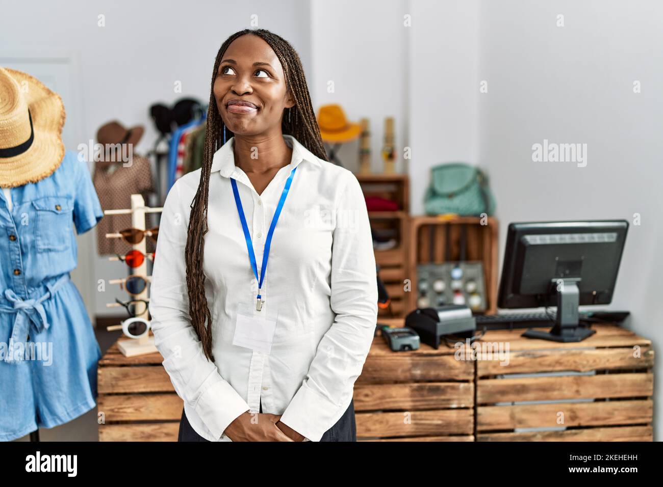 Black woman with braids working as manager at retail boutique smiling looking to the side and ...