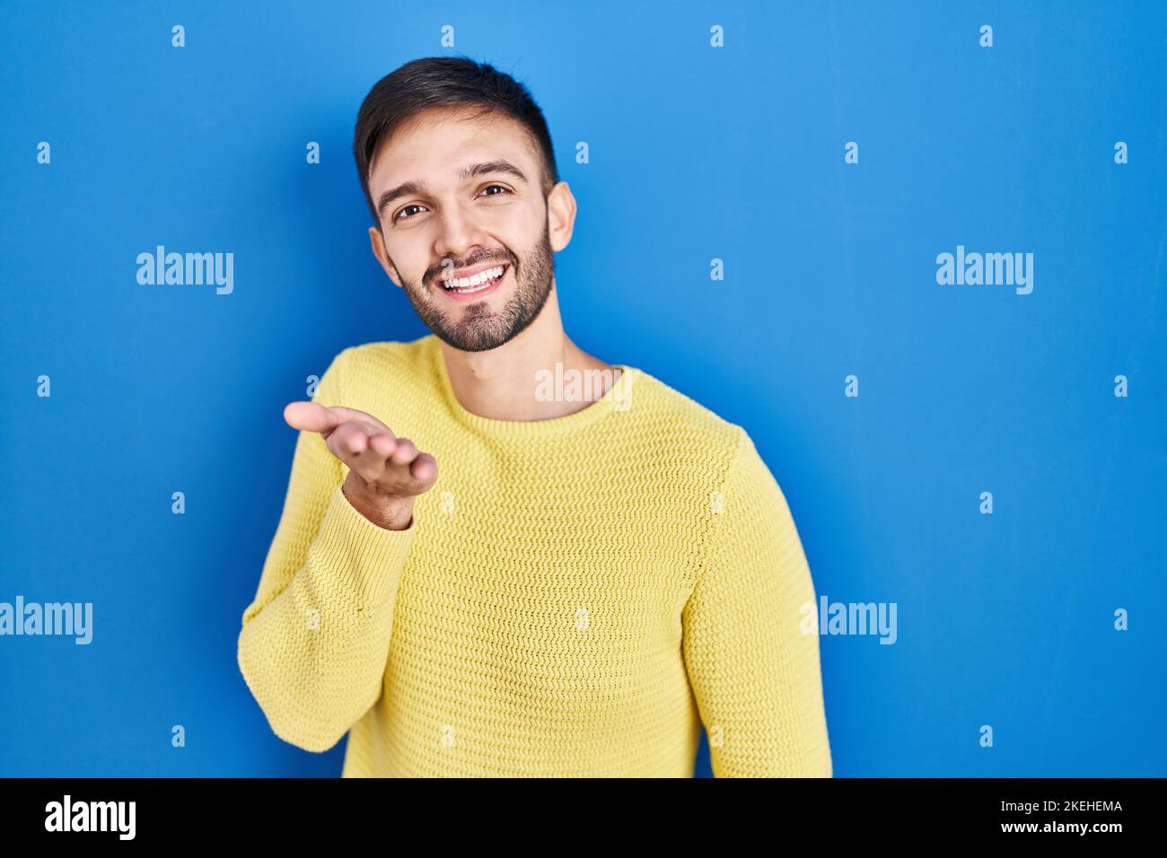 Hispanic man standing over blue background smiling cheerful offering ...