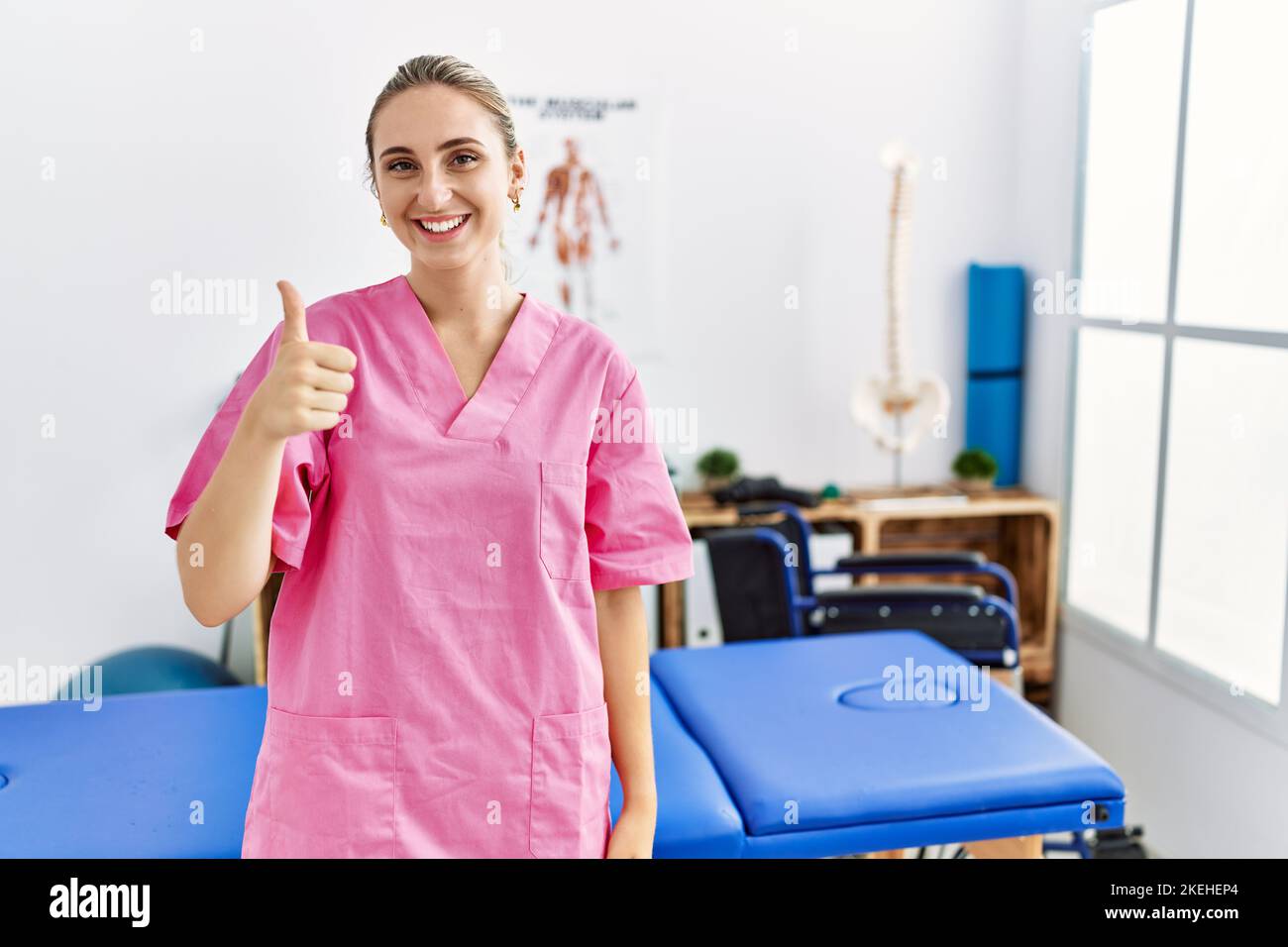 Young blonde woman working at pain recovery clinic doing happy thumbs ...