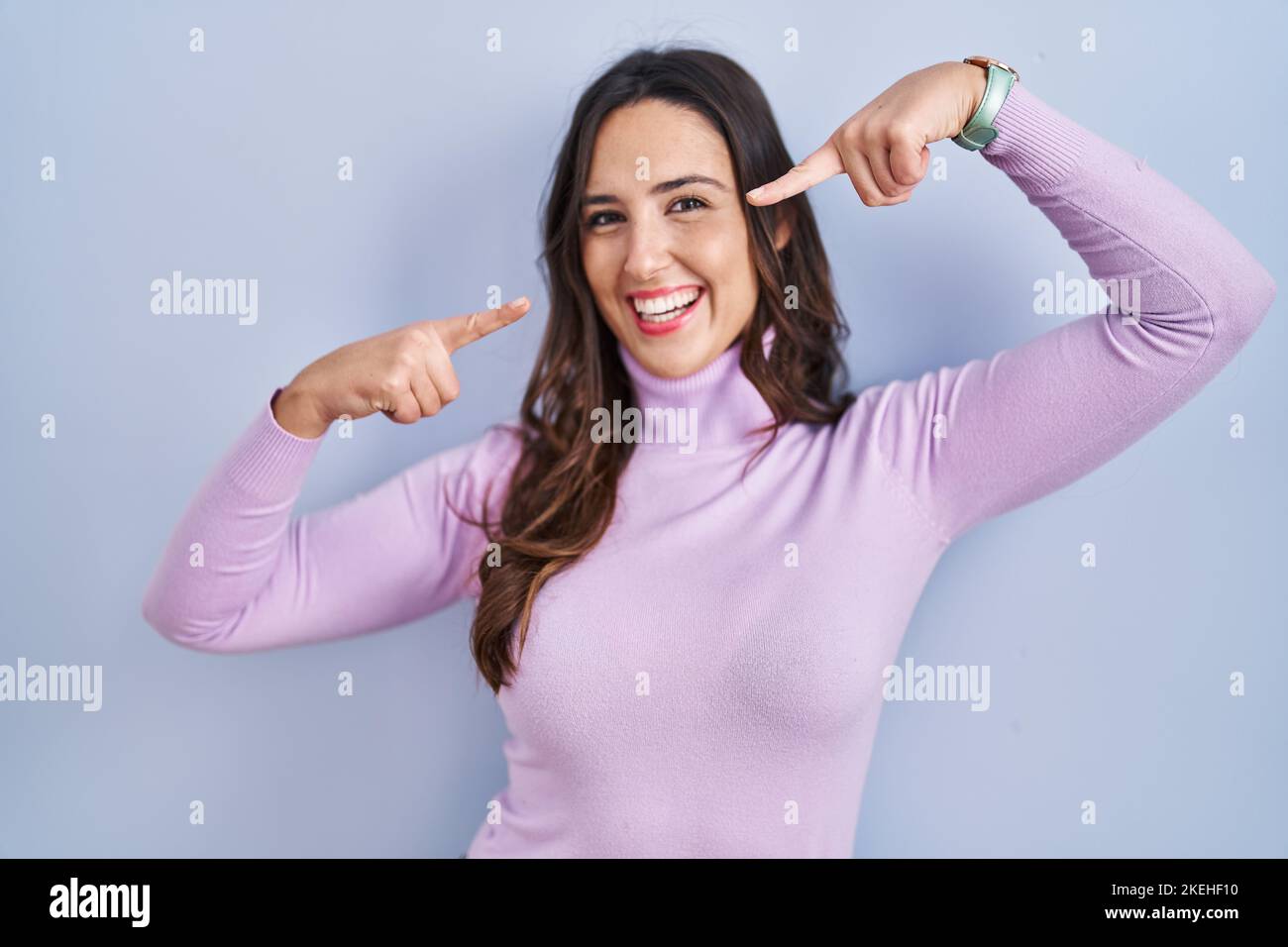 Young brunette woman standing over blue background smiling cheerful ...