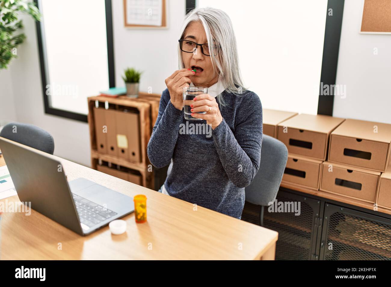 Middle age grey-haired woman business worker taking pills working at ...