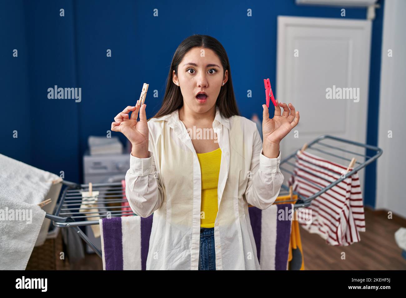 Young latin woman holding clothespins hanging clothes on clothesline in ...