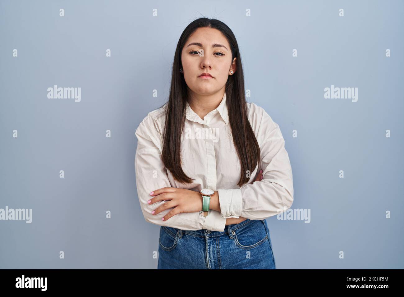 Young latin woman standing over blue background looking sleepy and ...