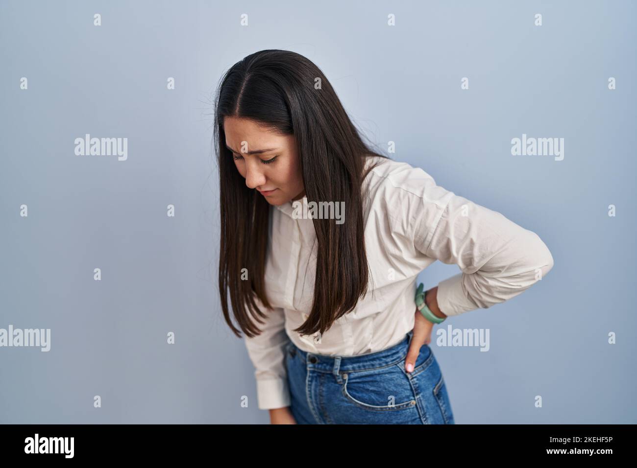 Young latin woman standing over blue background suffering of backache ...