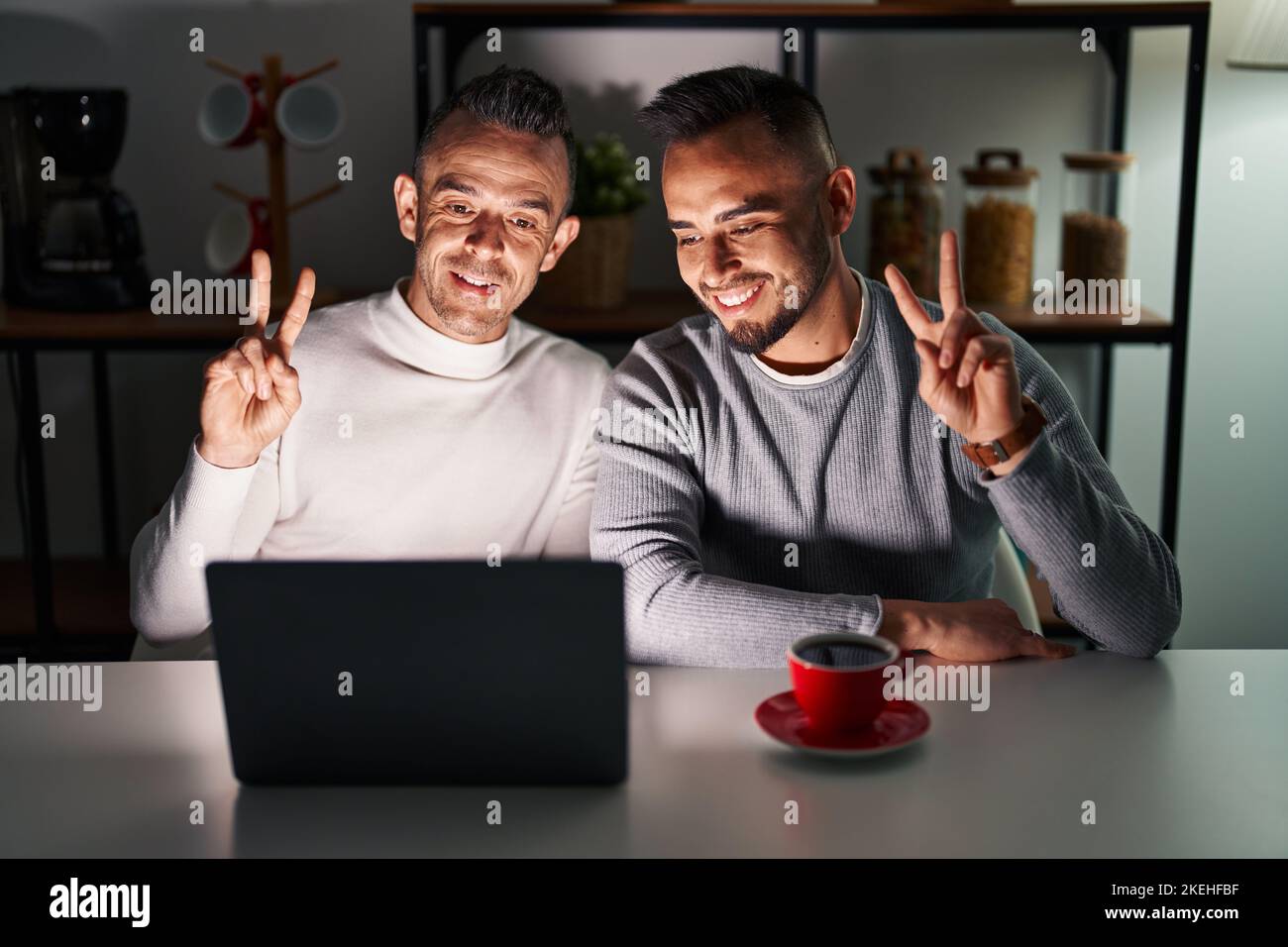 Homosexual couple using computer laptop smiling with happy face winking ...