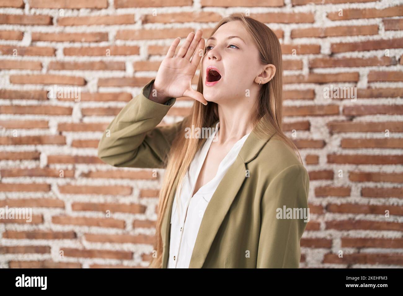 Young caucasian woman standing over bricks wall background shouting and ...