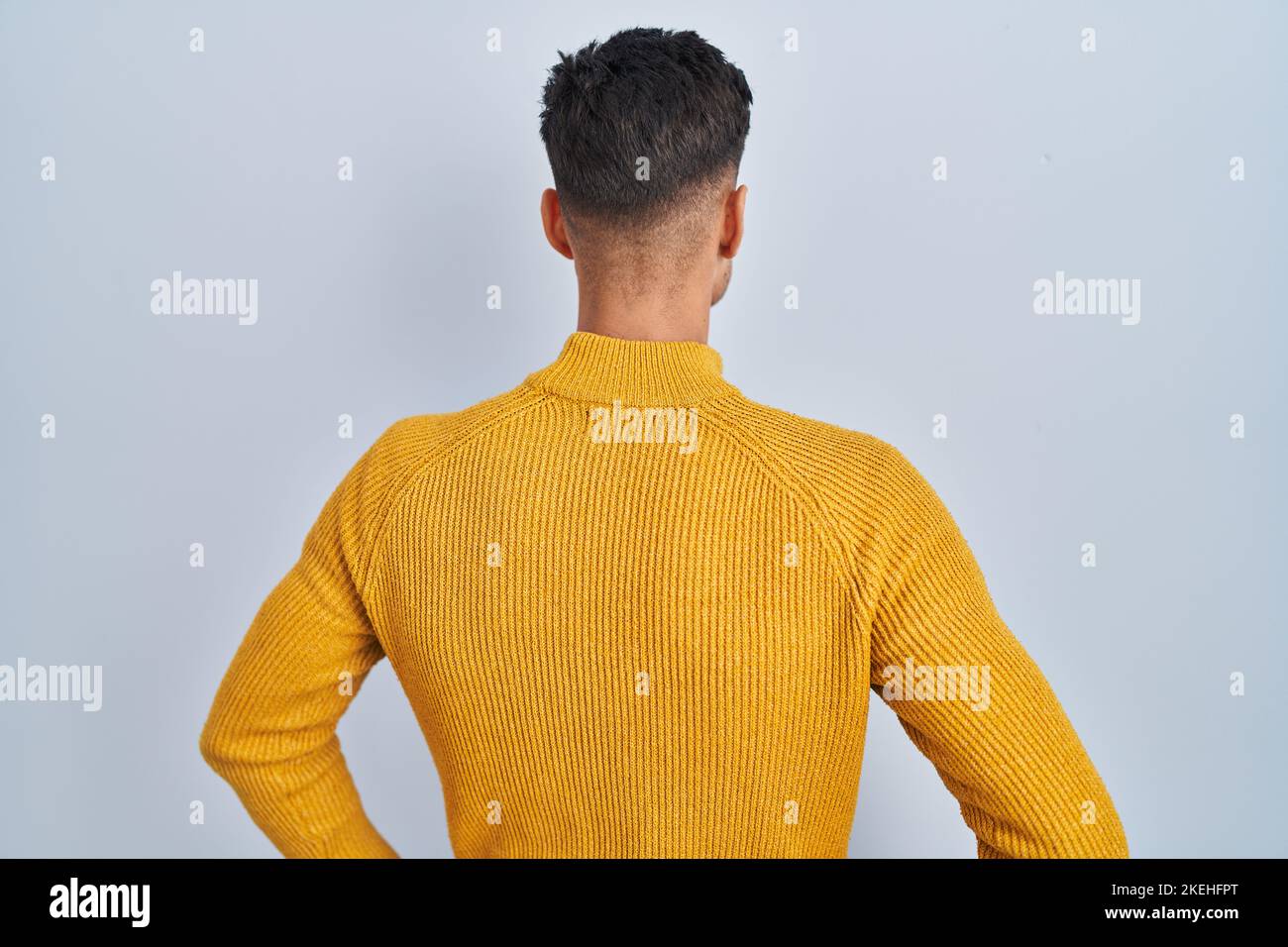 Young hispanic man standing over blue background standing backwards ...