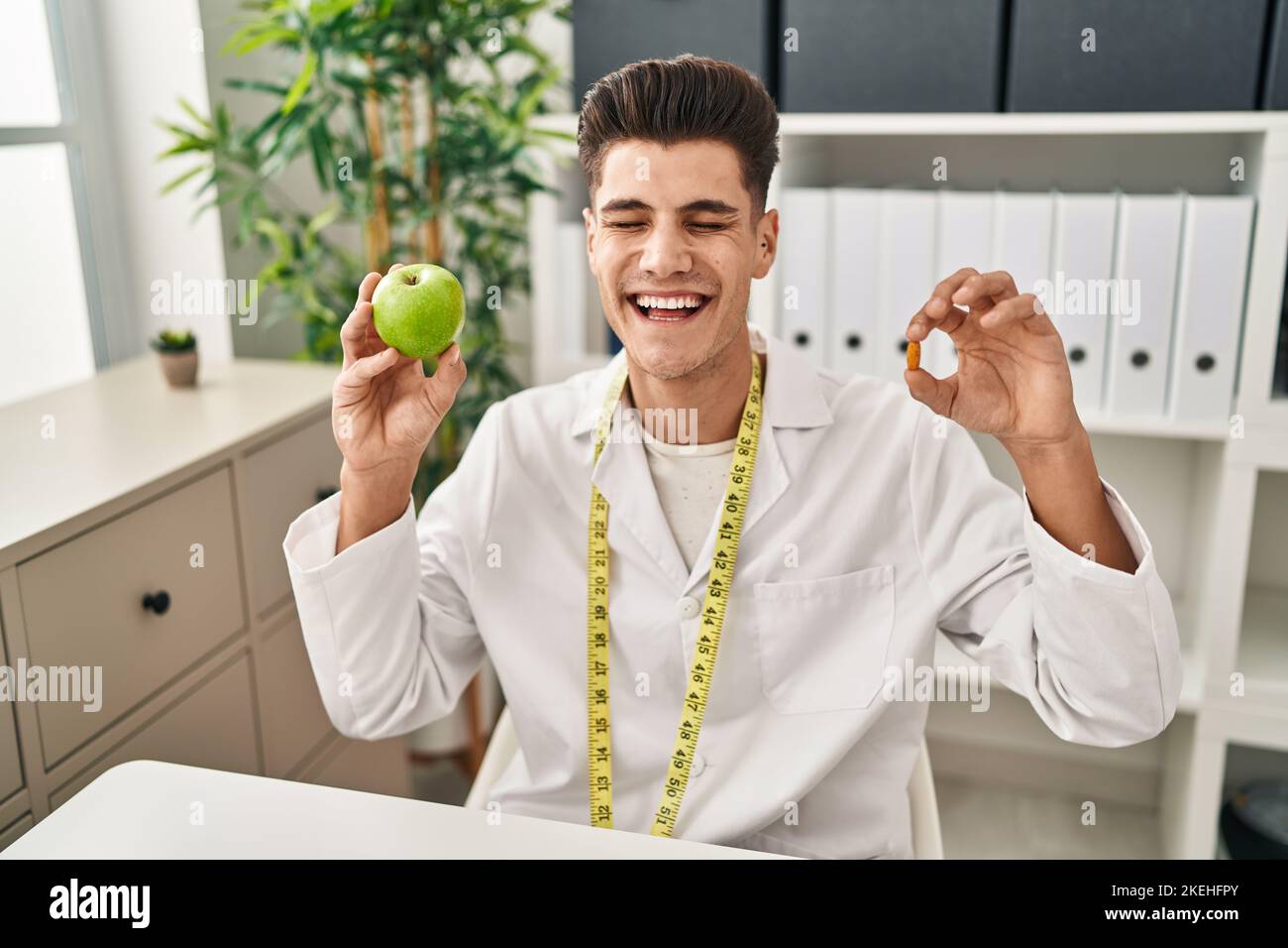 Young hispanic doctor man holding pills for fat loss smiling and ...