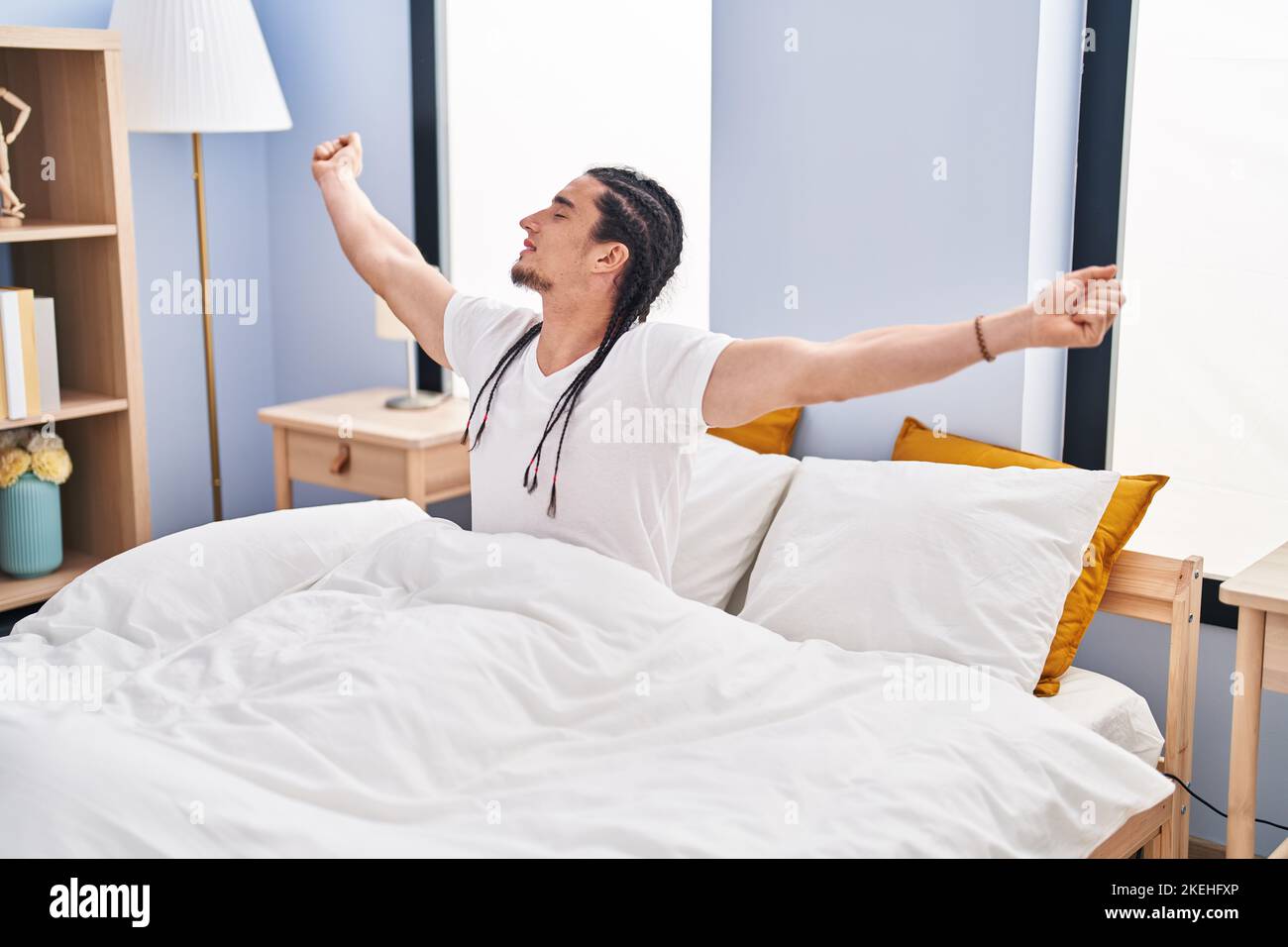 Young man stretching arms sitting on bed at bedroom Stock Photo - Alamy
