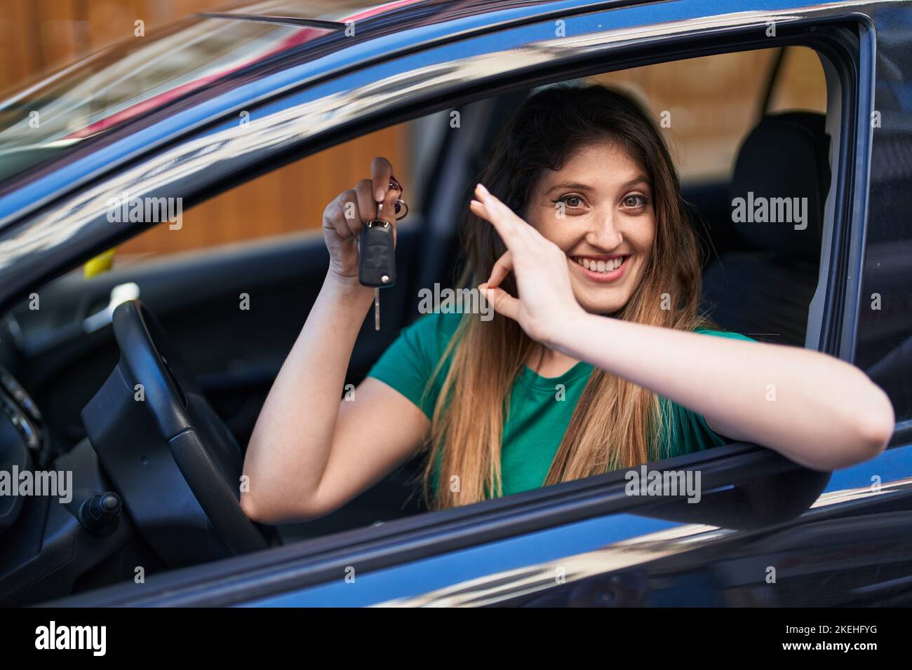 Young brunette woman holding key of new car doing ok sign with fingers ...