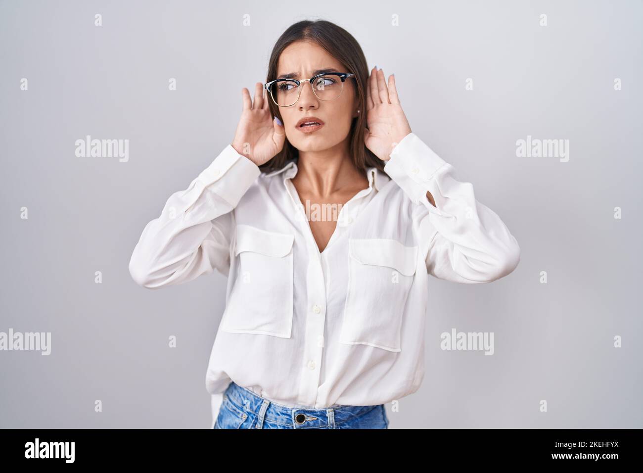 Young brunette woman wearing glasses trying to hear both hands on ear ...