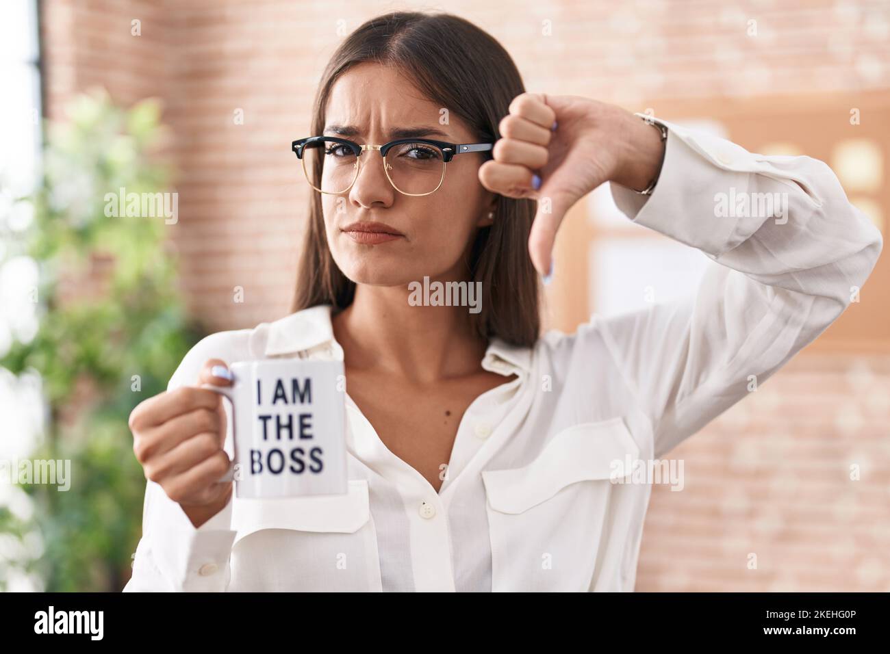 Young brunette woman drinking from i am the boss coffee cup with angry ...