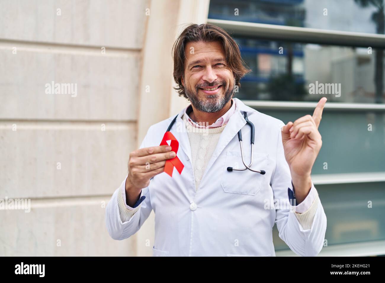 Handsome middle age doctor man holding support red ribbon smiling happy ...
