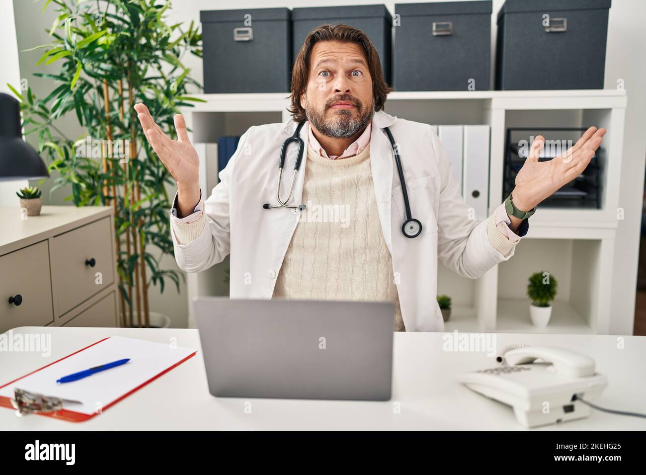 Handsome middle age doctor man working at the clinic clueless and ...
