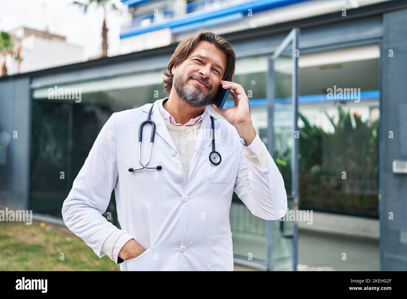 Middle age man doctor smiling confident talking on smartphone at ...
