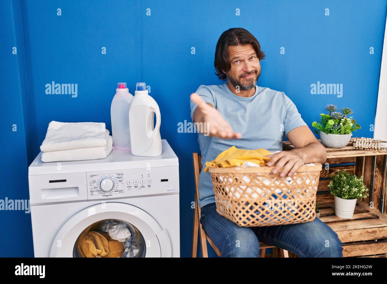Handsome middle age man waiting for laundry smiling friendly offering ...