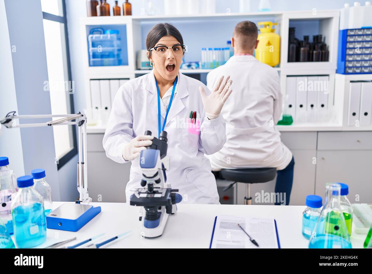 Young woman working at scientist laboratory scared and amazed with open ...