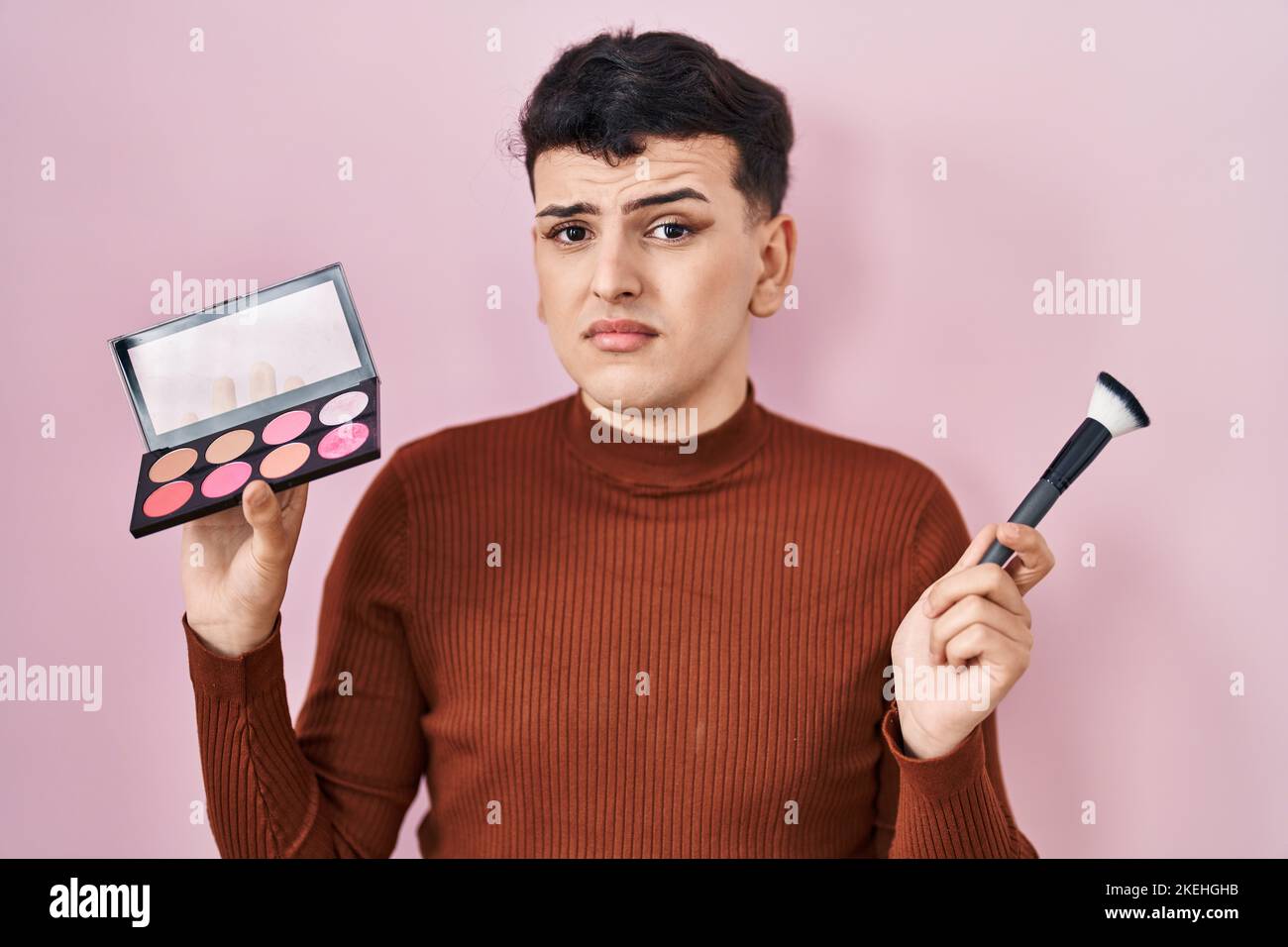 Non binary person holding makeup brush and blush clueless and confused ...
