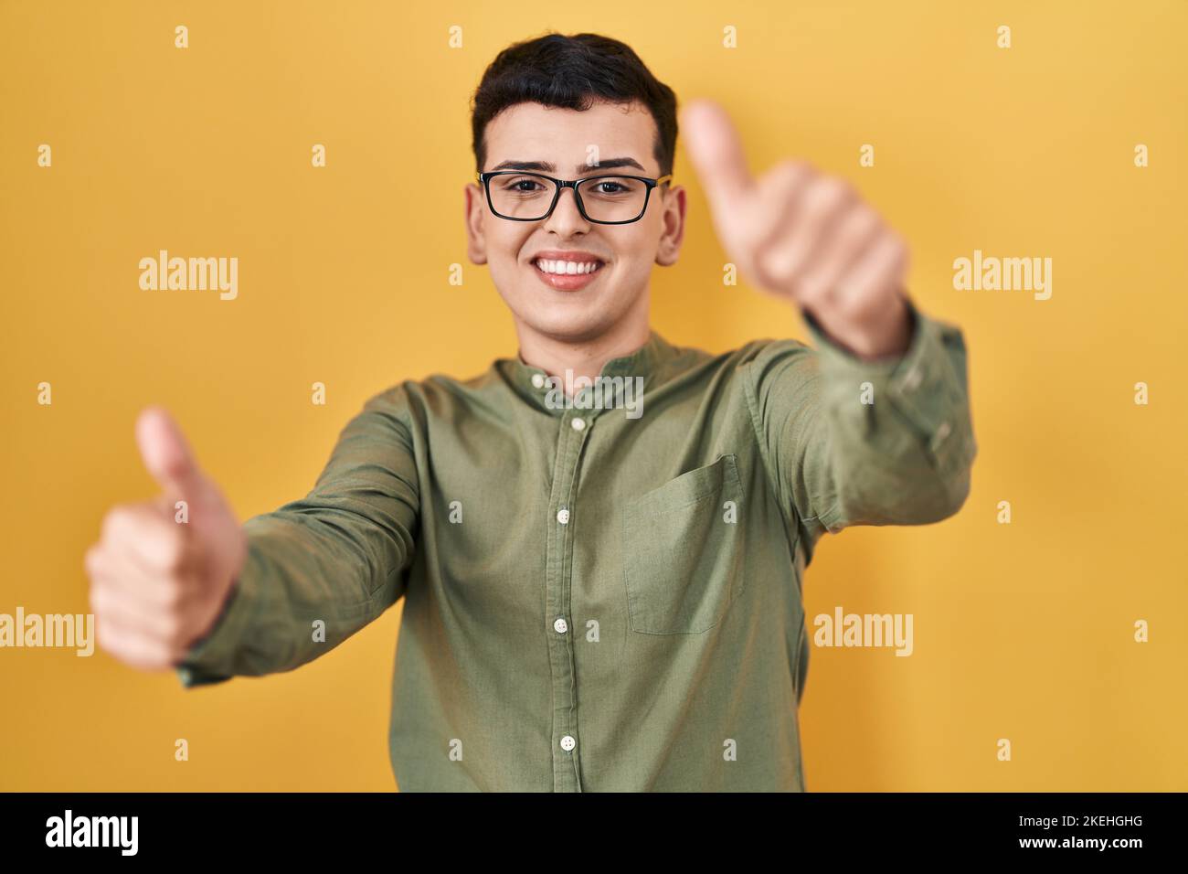 Non binary person standing over yellow background approving doing ...