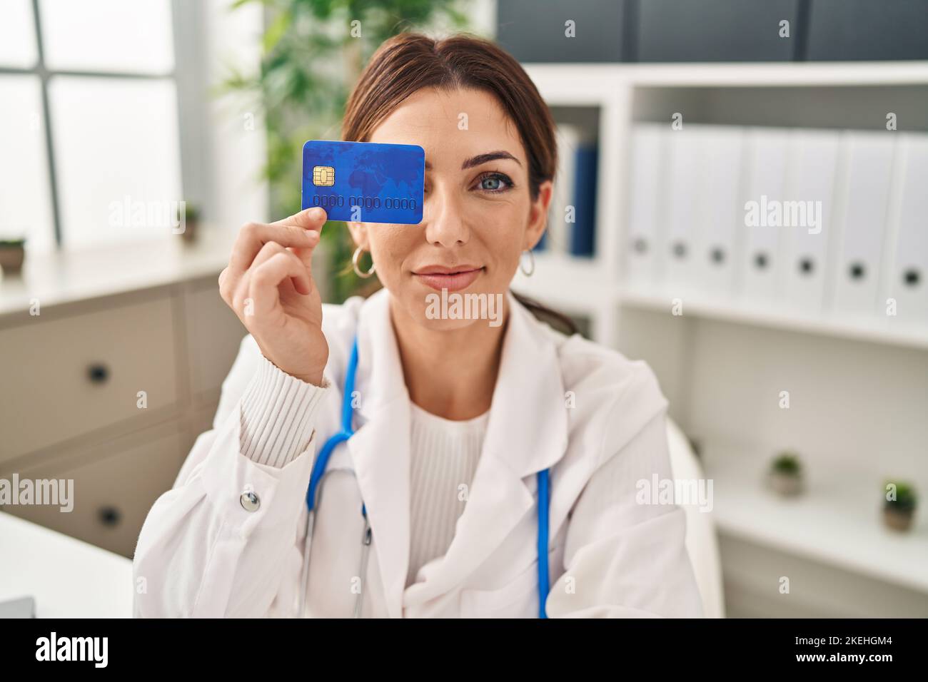 Young hispanic woman wearing doctor uniform holding credit card over ...