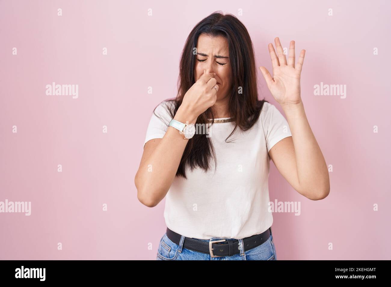 Young brunette woman standing over pink background smelling something ...