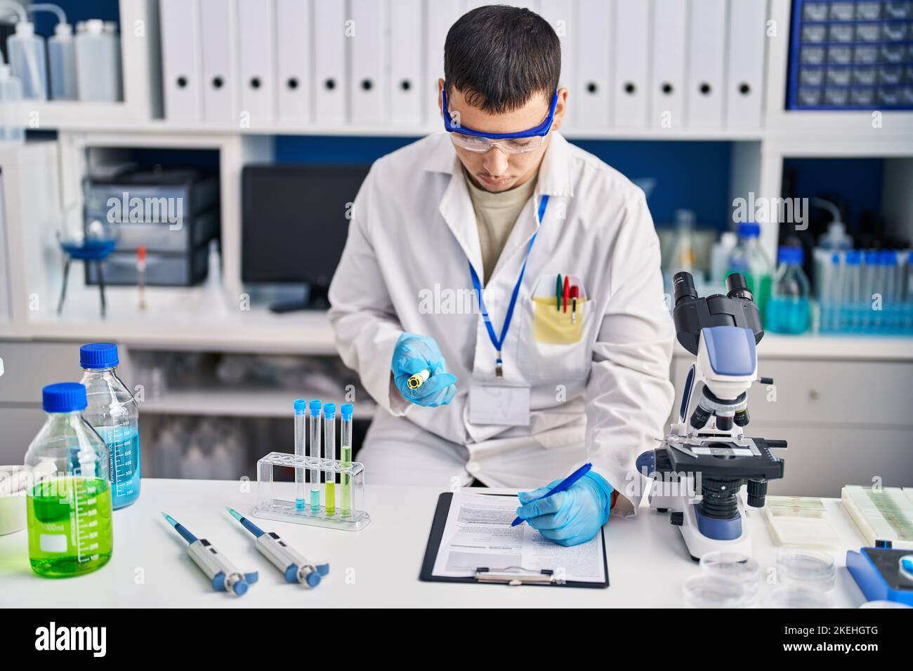 Young man scientist writing on document measuring liquid at laboratory ...