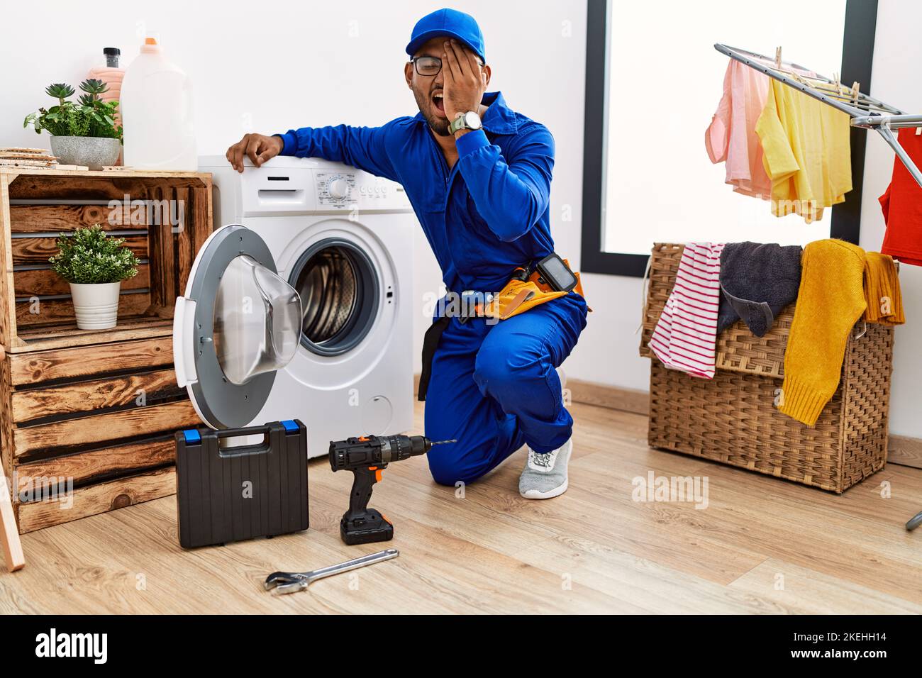 Young indian technician working on washing machine yawning tired ...