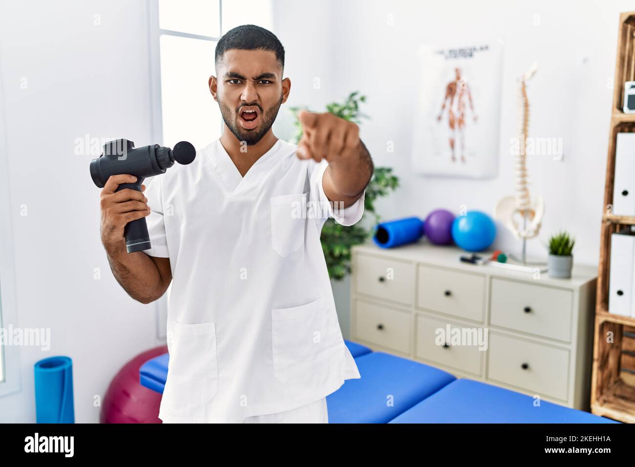 Young indian physiotherapist holding therapy massage gun at wellness ...