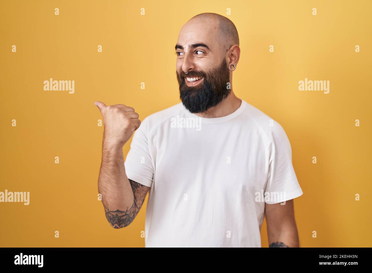 Young hispanic man with beard and tattoos standing over yellow ...