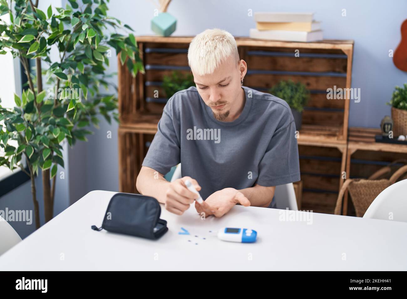 Young caucasian man measuring glucose sitting on table at home Stock ...