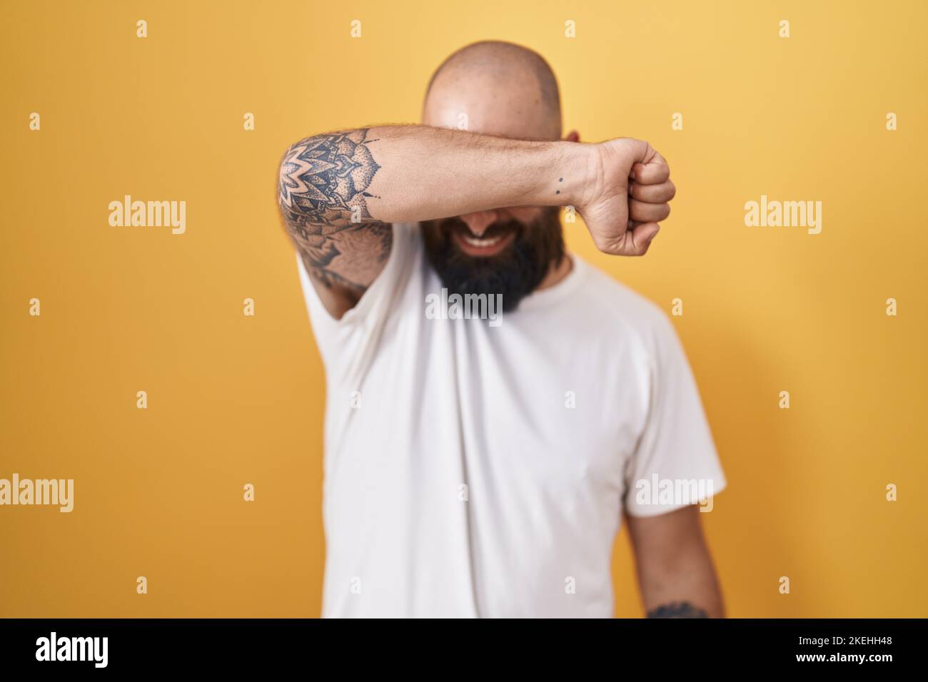 Young hispanic man with beard and tattoos standing over yellow ...