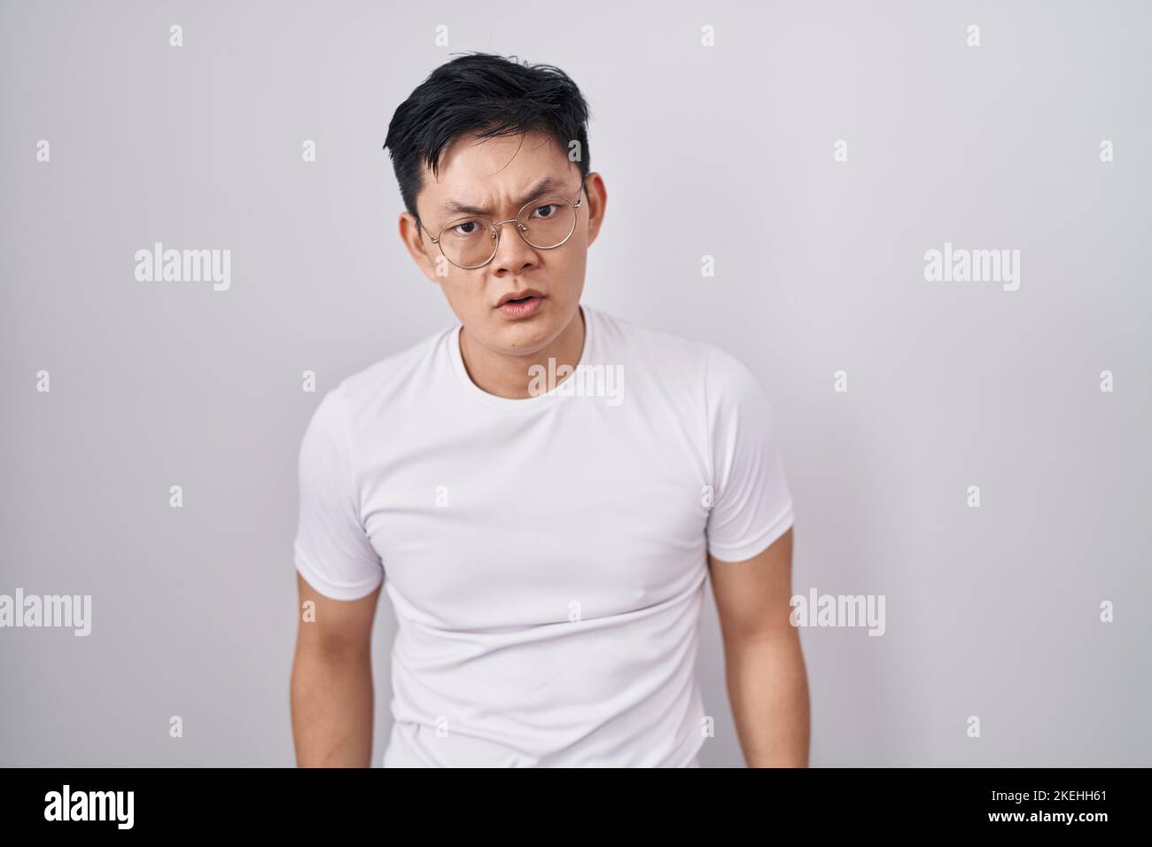 Young asian man standing over white background in shock face, looking ...