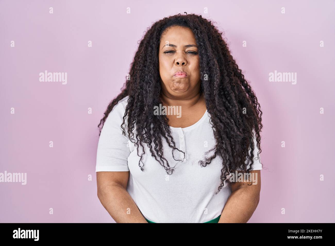 Plus size hispanic woman standing over pink background puffing cheeks ...