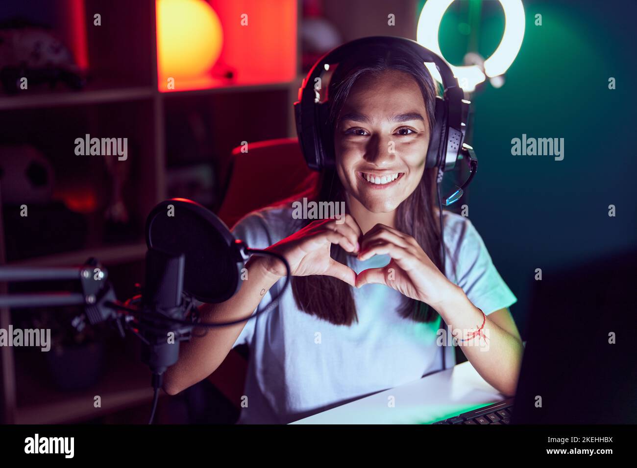 Young beautiful hispanic woman streamer smiling confident doing heart ...