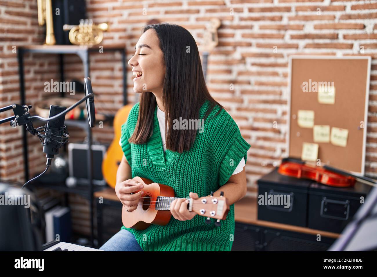 Young hispanic woman musician singing song playing ukulele at music ...