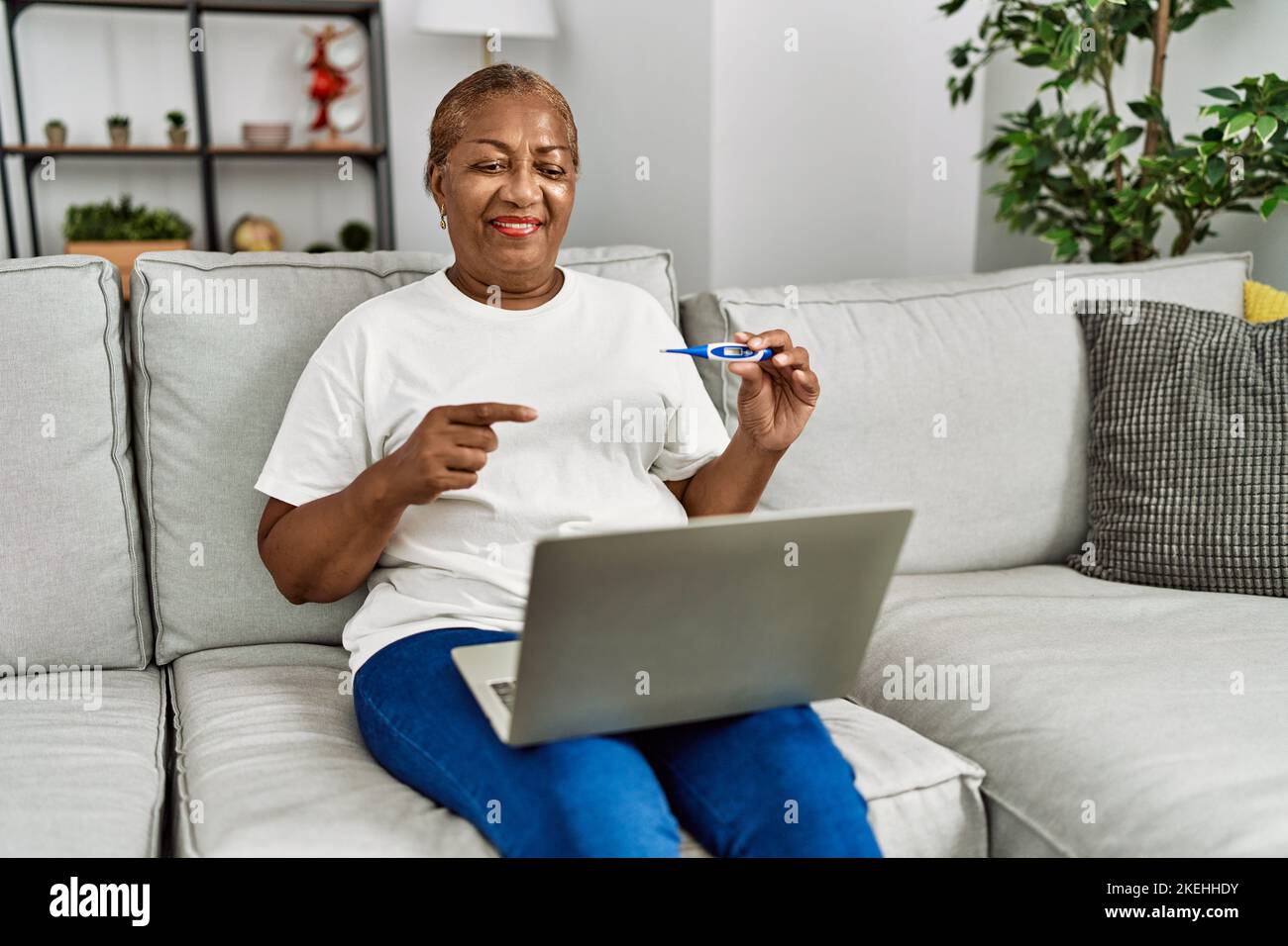 Senior african american woman having telemedicine measuring temperature ...