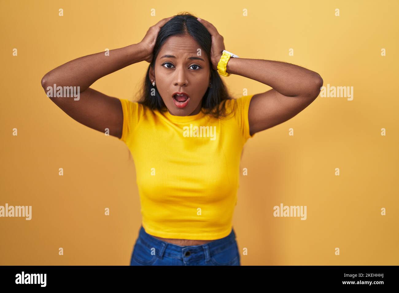Young indian woman standing over yellow background crazy and scared ...
