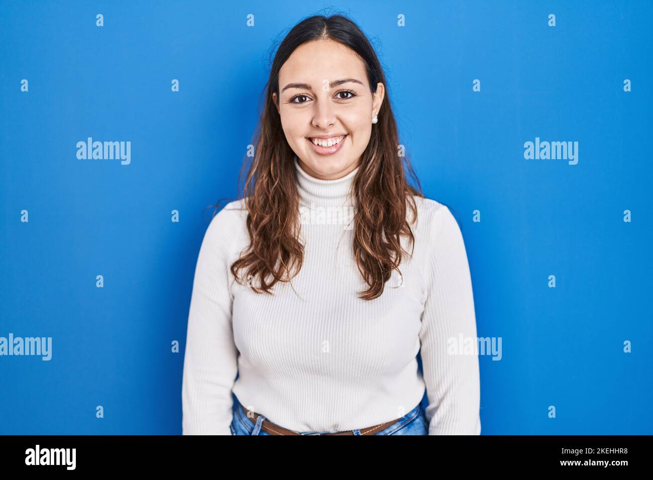 Young hispanic woman standing over blue background with a happy and ...