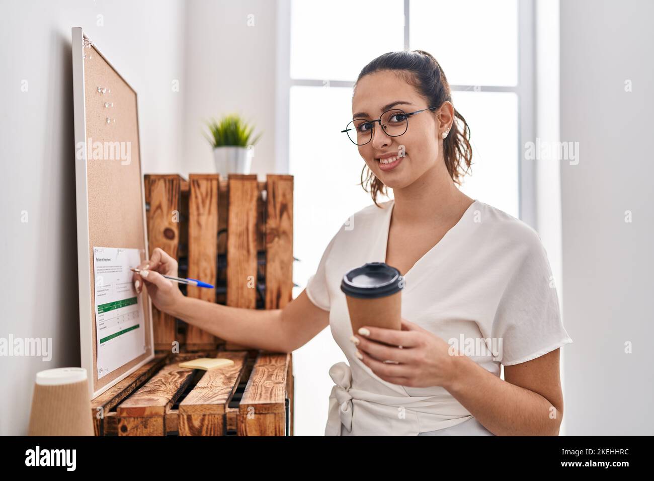 Young beautiful hispanic woman business worker writing on cork board ...