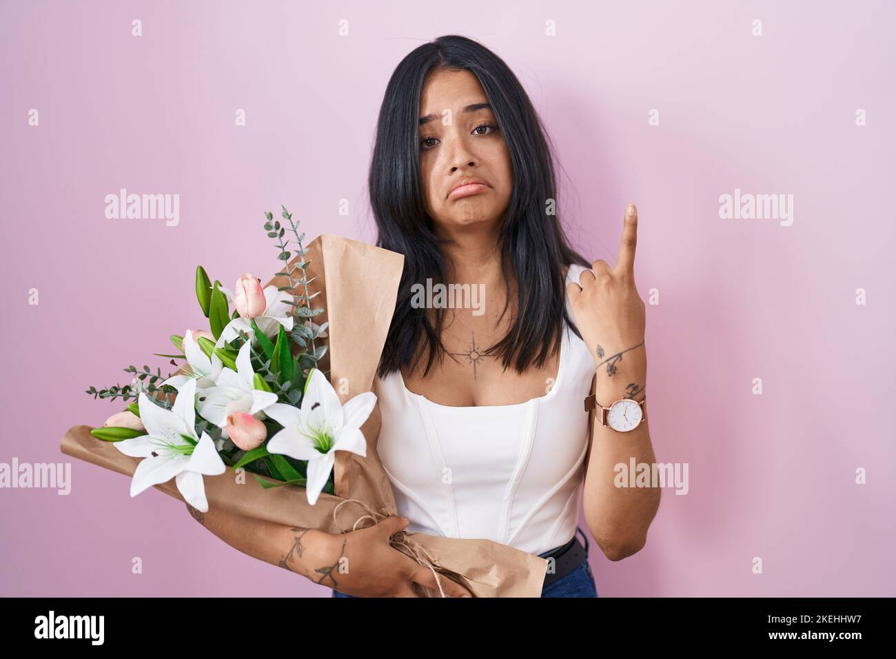 Brunette woman holding bouquet of white flowers pointing up looking sad ...