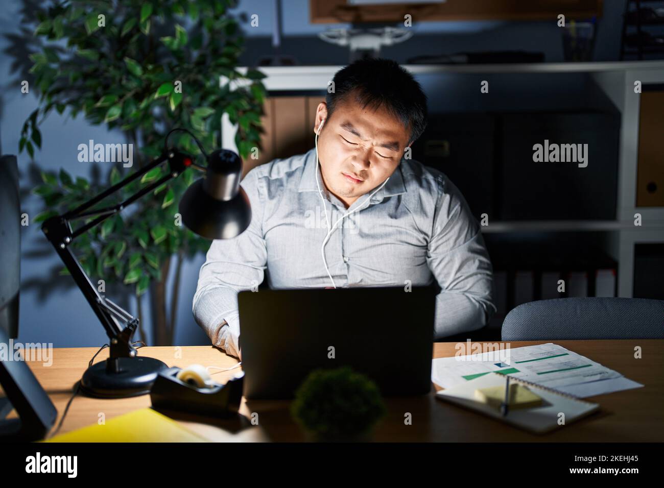 Young chinese man working using computer laptop at night with hand on ...